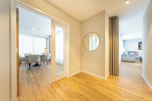 Um interior moderno com soalho de madeira, área de refeições com cadeiras e mesa, sala de estar com sofá e um espelho grande na parede.