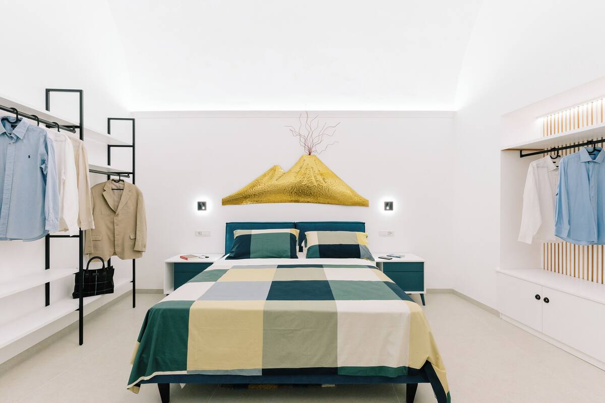 Quarto moderno com cama, mesas de cabeceira, guarda-roupa e cabideiro.