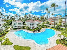 Um resort com uma grande piscina, edifícios de vários andares e palmeiras.