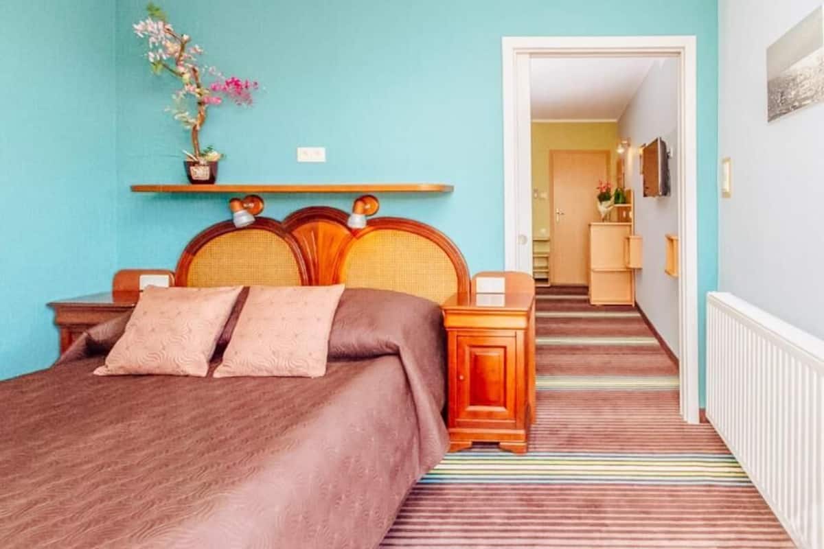 Quarto com cama, mesa de cabeceira, abajur e uma pequena prateleira com uma planta.
