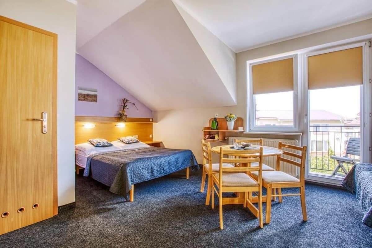 Um quarto com cama, escrivaninha e cadeira, janela com vista e porta.
