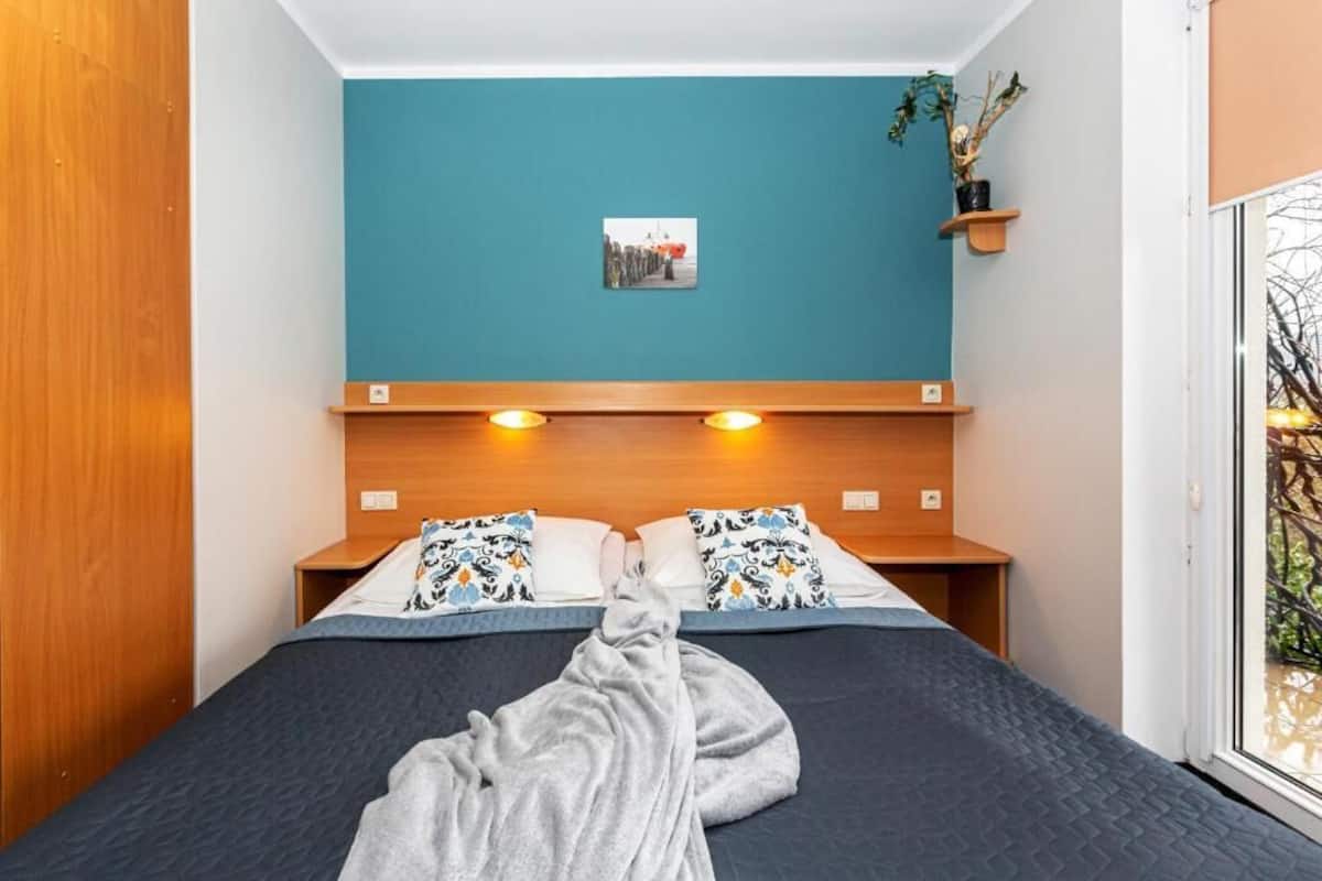Quarto com cama, duas mesas de cabeceira, prateleira na parede com uma planta e uma janela.
