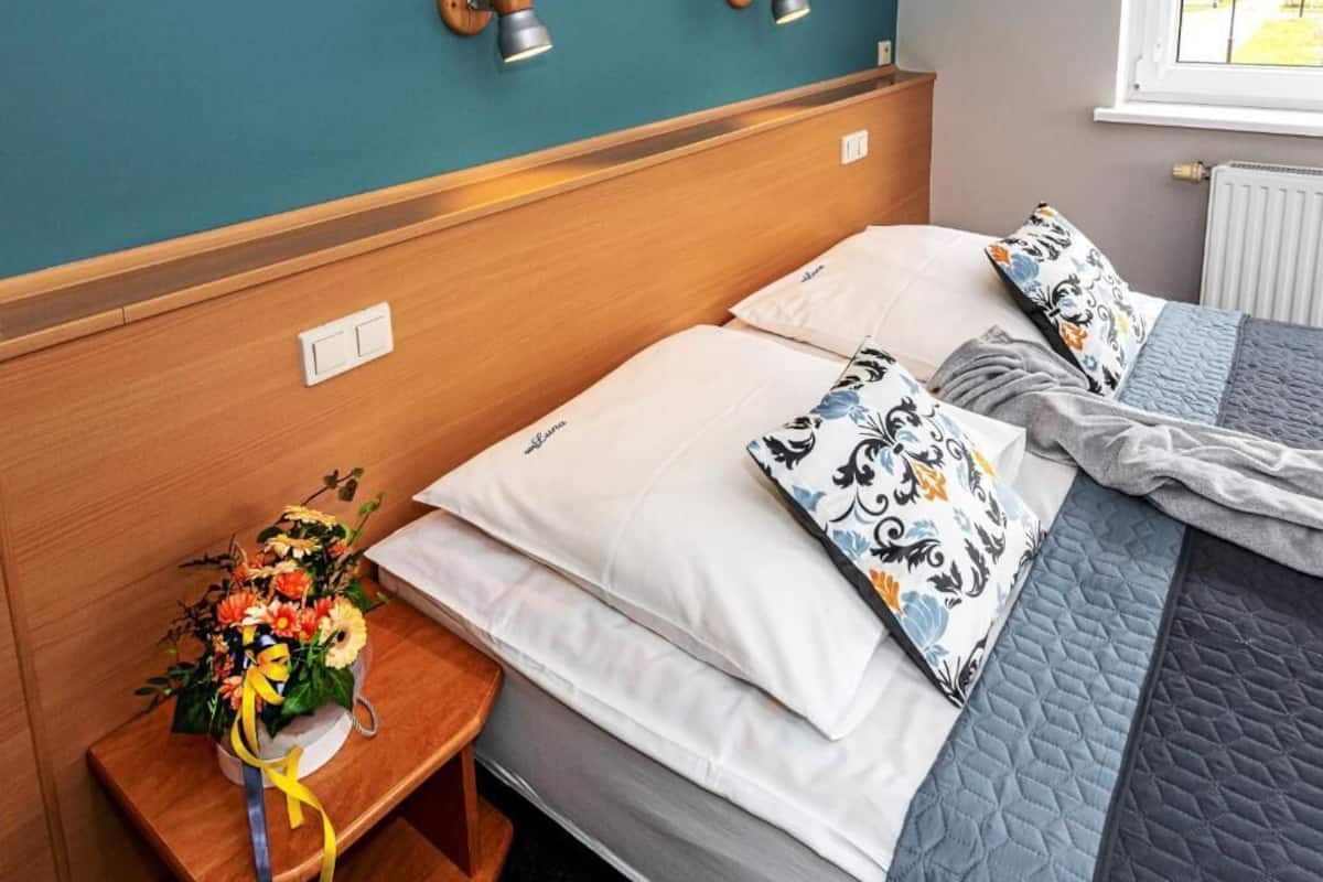Quarto de hotel com cabeceira de madeira, duas camas com roupa de cama estampada e lisa, mesa de cabeceira com arranjo floral e luminárias fixadas na parede.
