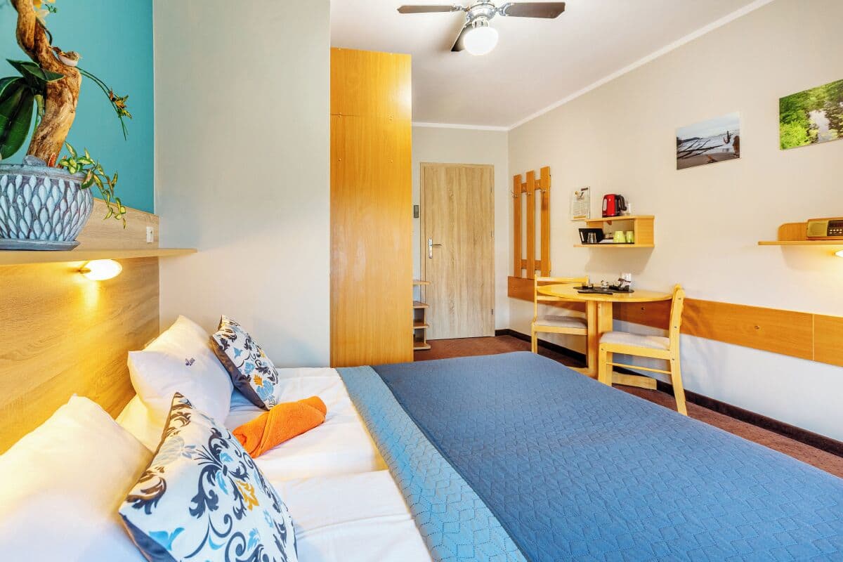 Quarto de hotel com cama, escrivaninha, cadeira, planta em vaso e vista para o exterior.