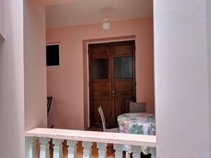 Quarto com porta de madeira, uma pequena janela e uma varanda com guarda-corpo branco.