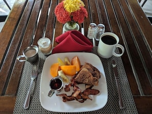 Prato de café da manhã com frutas, bacon e café sobre mesa de madeira.