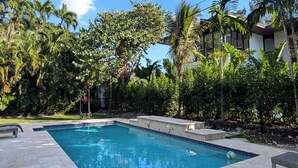Piscina com bordas azulejadas, rodeada por palmeiras e um céu azul límpido.