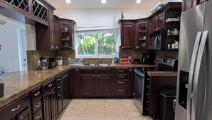 Cozinha moderna com armários de madeira escura, bancadas de granito, geladeira de aço inoxidável e uma ilha grande com pia.