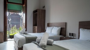 Quarto de hotel com duas camas, um guarda-roupa de madeira e uma varanda com vista para edifícios.