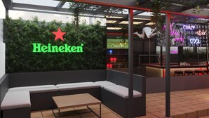 Uma área de estar ao ar livre com a marca Heineken, design moderno, incluindo um sofá e uma mesa.