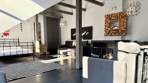 Quarto moderno estilo loft com cama, sofá, lareira e área de refeições.