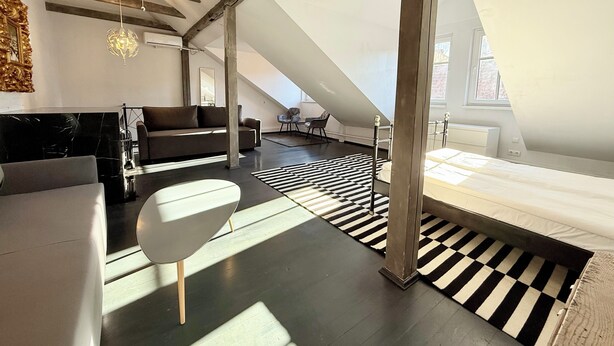 Um loft moderno com teto alto, vigas aparentes, tapete listrado em preto e branco, sofá e área de jantar.