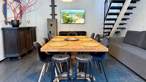 Uma área de refeições moderna com mesa de madeira, cadeiras pretas, luminária pendente preta, uma TV na parede e uma escada.