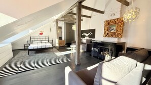 Um quarto de sótão com teto inclinado, cama, sofá, lareira e um espaço de jantar.