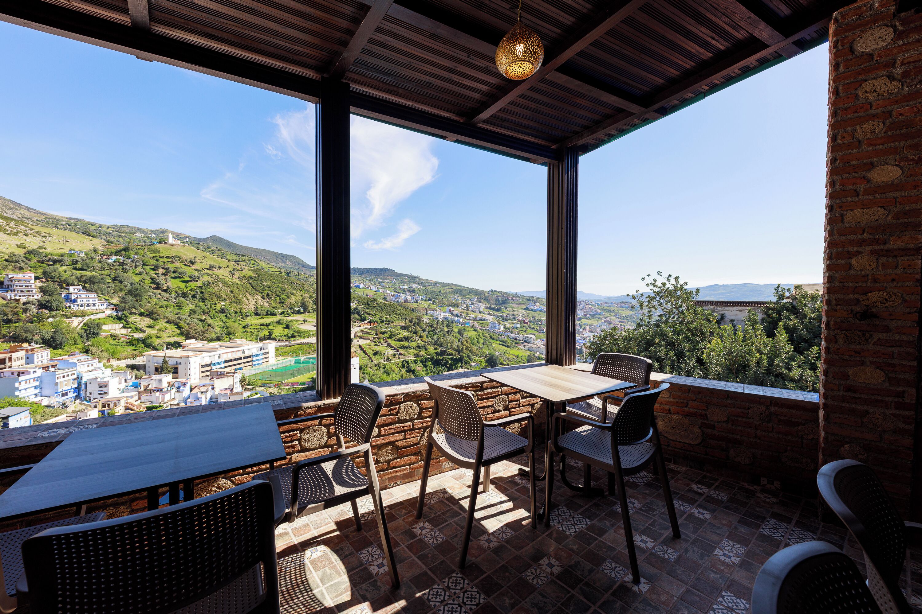 Terraço com mesa e cadeiras, dando vista para um vale com edifícios e vegetação.