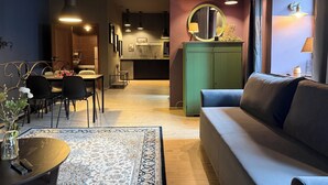 Uma sala de estar moderna com um sofá, área de jantar com cadeiras, uma cozinha ao fundo e iluminação pendente.