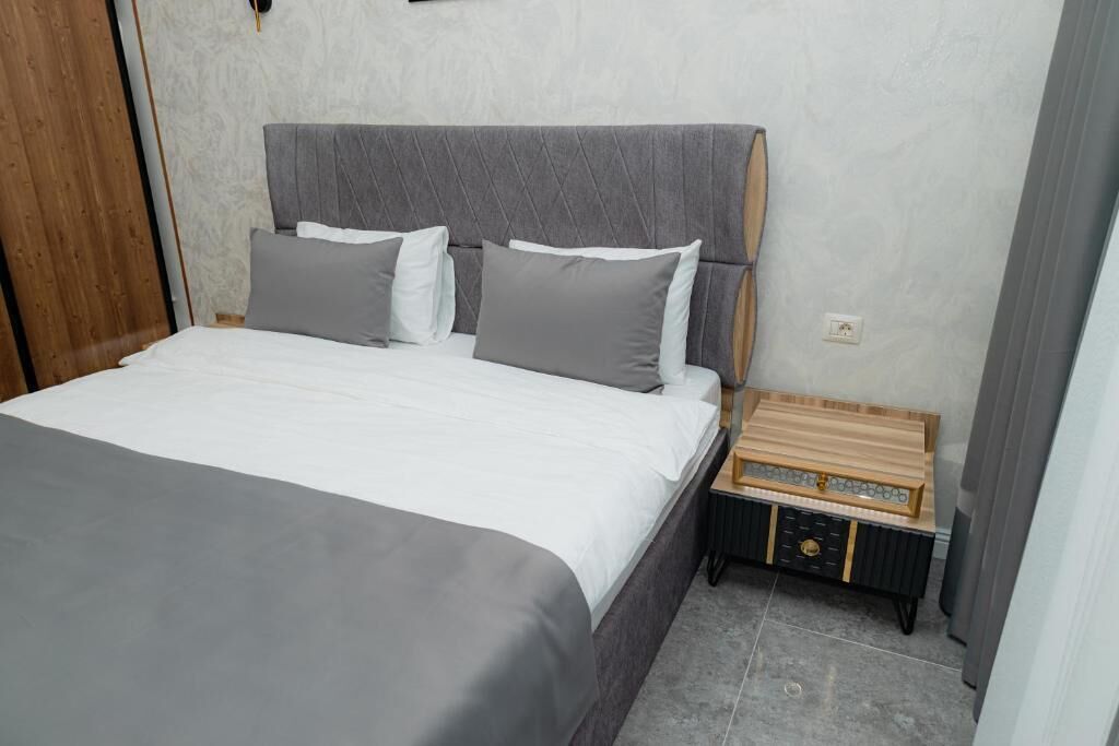 Quarto com cama, almofadas, mesa de cabeceira e mesa lateral de madeira.