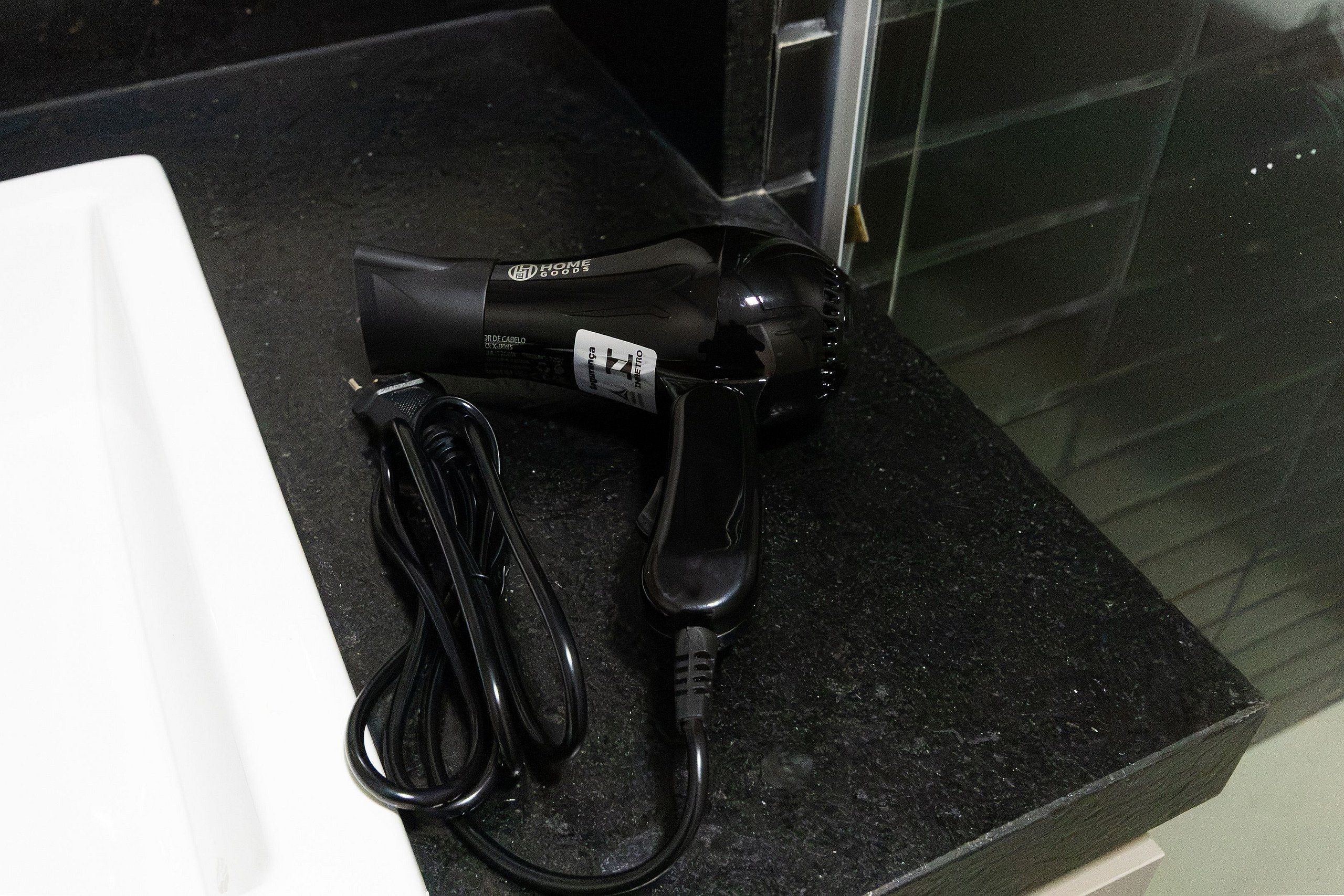 Secador de cabelo preto com fio sobre bancada preta.