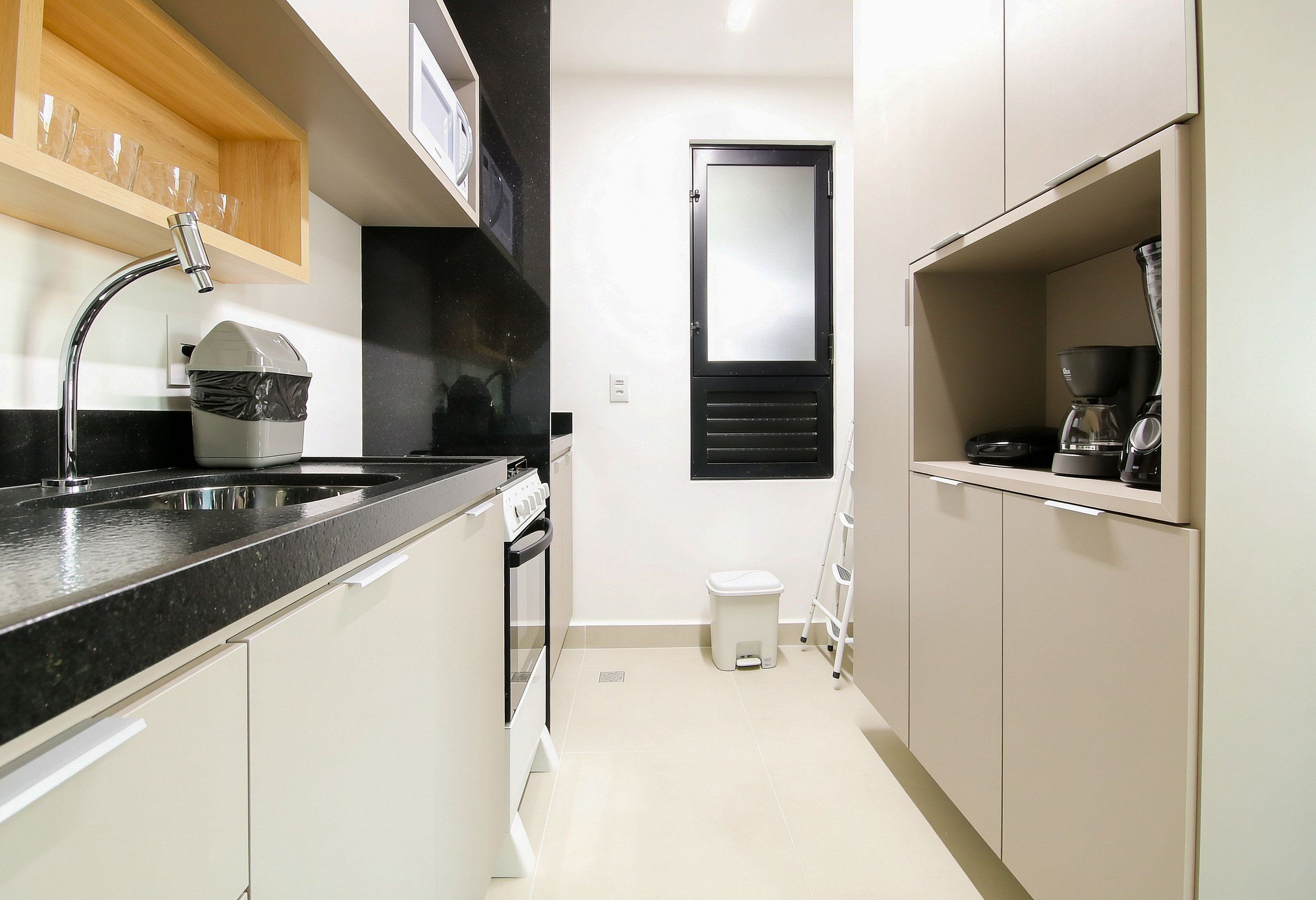 Cozinha compacta com bancada preta, pia de aço inoxidável e máquina de café.