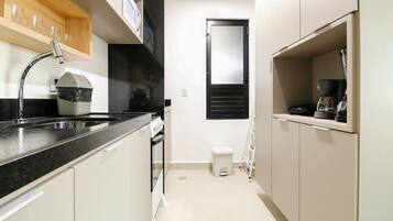 Cozinha compacta com bancada preta, pia de aço inoxidável e máquina de café.