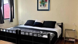 Quarto de hotel com cama, mesa de cabeceira, um quadro pendurado na parede e uma janela com cortinas.