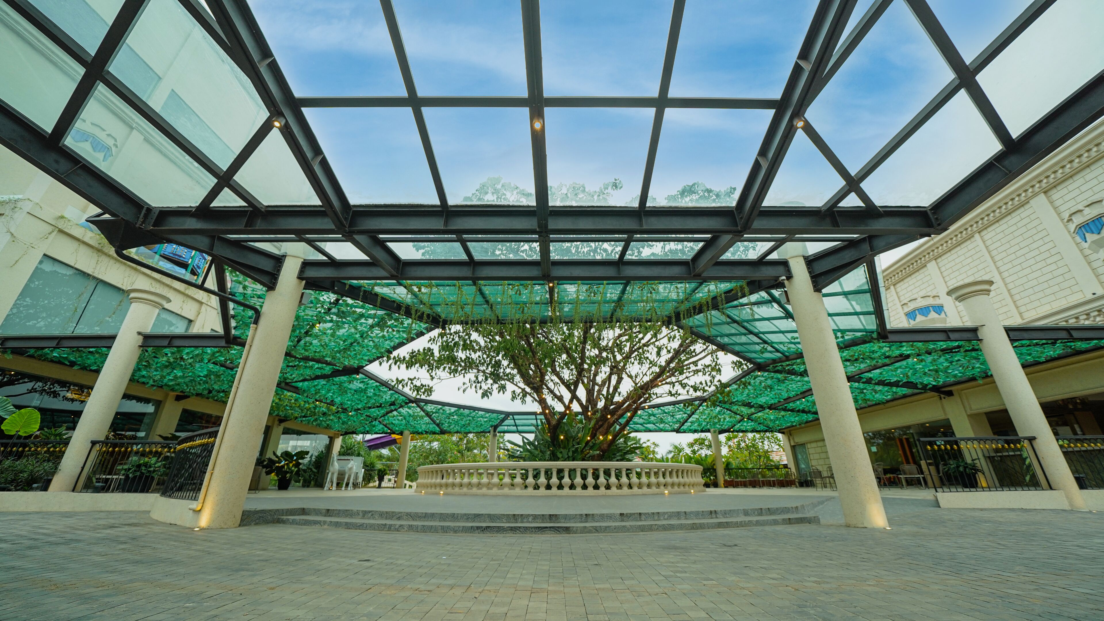 Uma galeria coberta com teto de vidro, colunas e um jardim central.