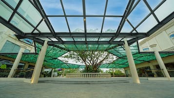 Uma galeria coberta com teto de vidro, colunas e um jardim central.