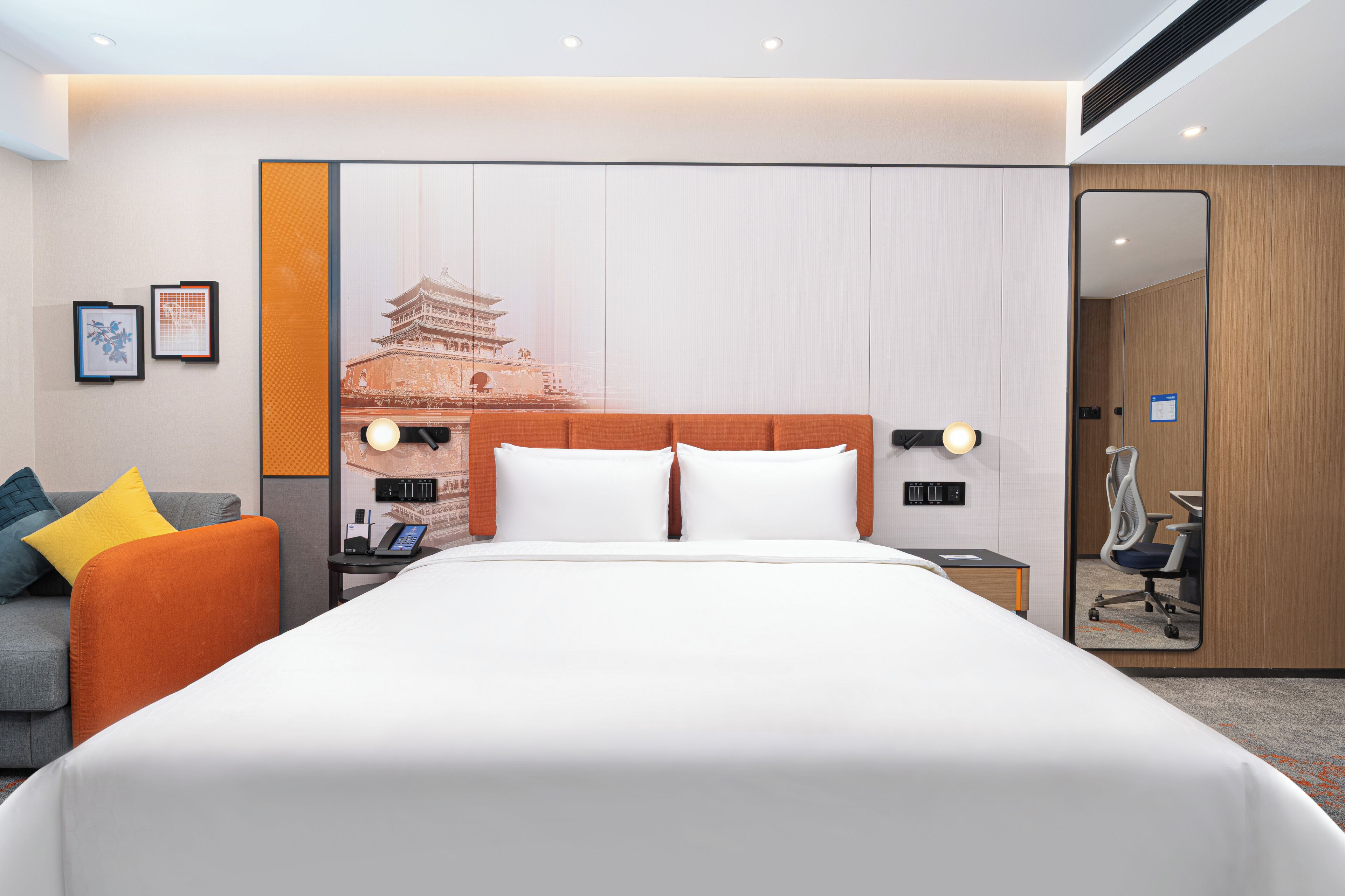 Quarto de hotel com uma cama grande, um sofá, uma escrivaninha e um espelho.