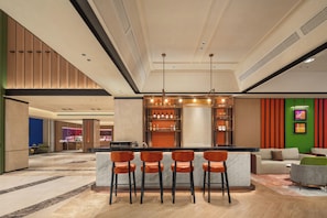 Um hall de hotel moderno com área de bar, assentos e balcão de recepção.
