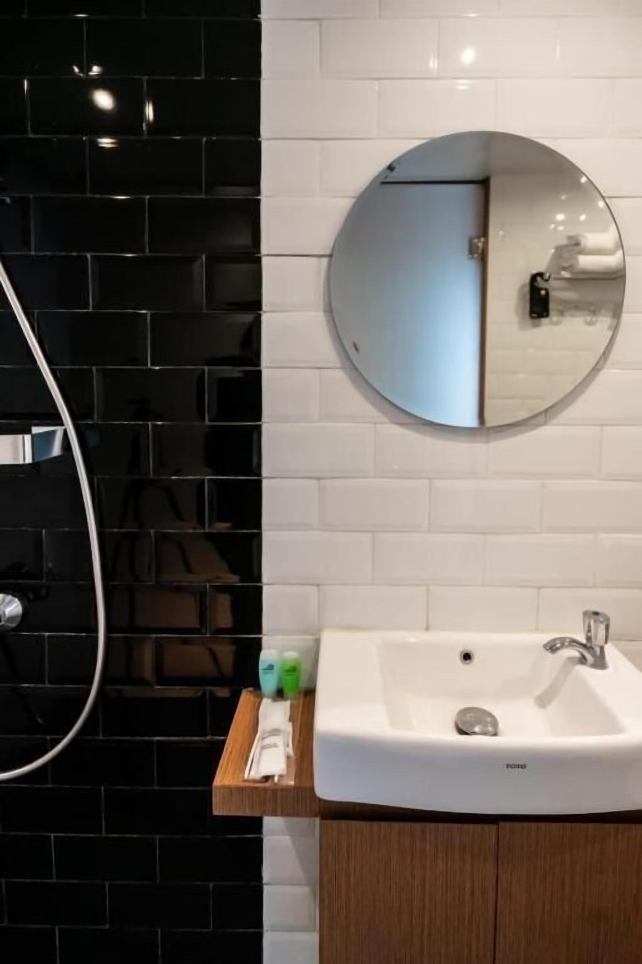 Um banheiro com pia branca, espelho redondo e parede revestida com azulejos pretos.