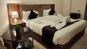 Quarto de hotel com cama, mesa de cabeceira com abajur, mesa redonda com planta e um quadro na parede.