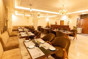 Uma sala de jantar com várias mesas e cadeiras, uma estátua de Buda e um candelabro.