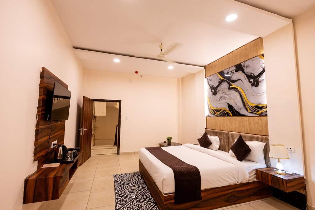Quarto de hotel moderno com uma cama grande, televisão de tela plana, cabeceira de madeira e ventilador de teto.
