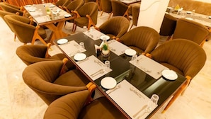 Uma sala de jantar com mesas redondas, cadeiras e toalhas de mesa bem postas.