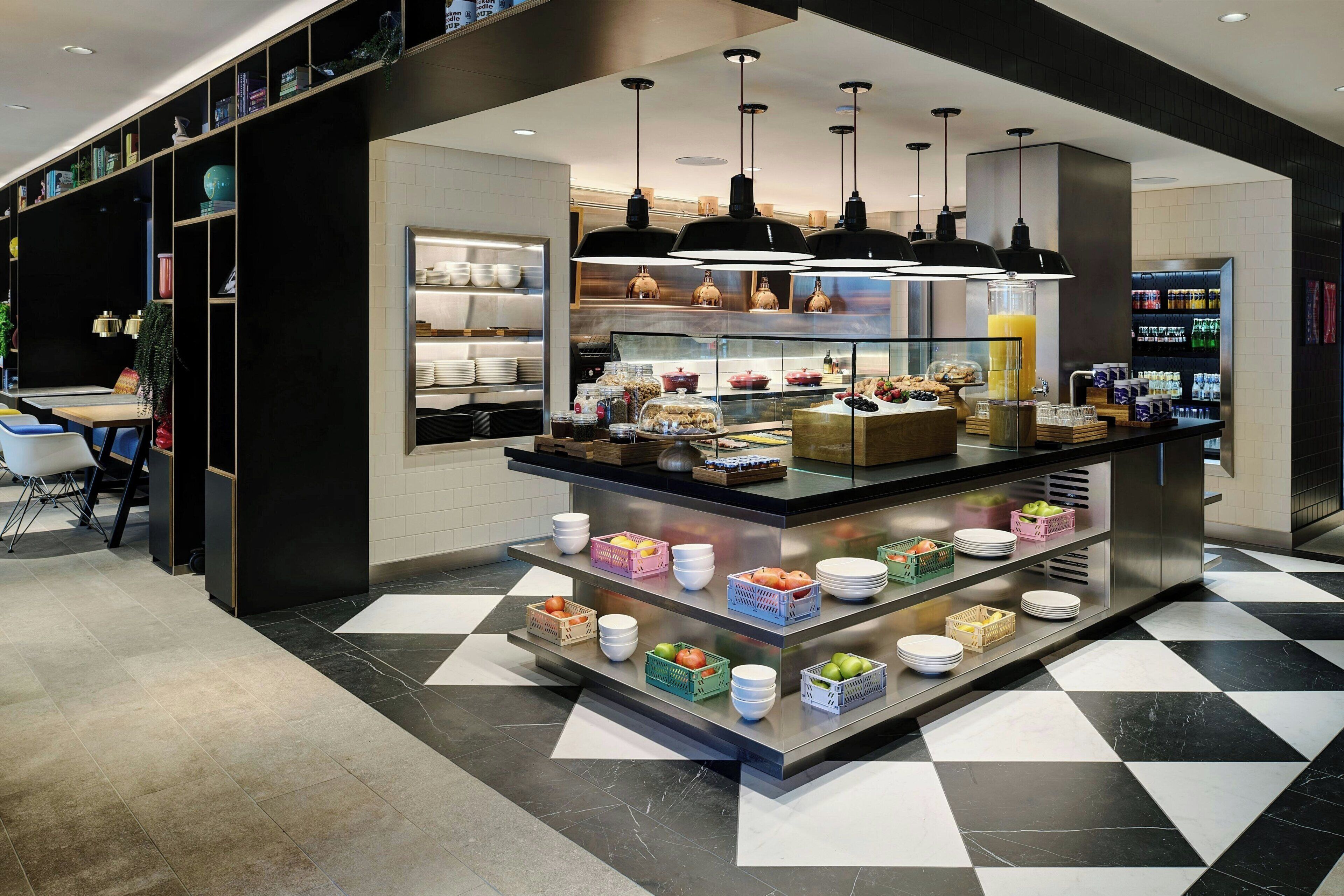 Um balcão de café da manhã moderno, com diversas opções de comida e bebidas, rodeado por estantes com livros e objetos decorativos.