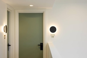 Entrada de um quarto de hotel, com porta, luminária e placa indicando 'SUITE 08'.