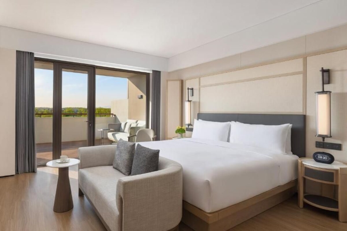 Quarto de hotel com cama, sofá, mesa pequena, televisão e varanda com área de estar.