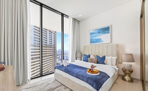 Quarto de hotel moderno com uma cama grande, vista para a cidade, porta deslizante e paisagem urbana visível pela janela.