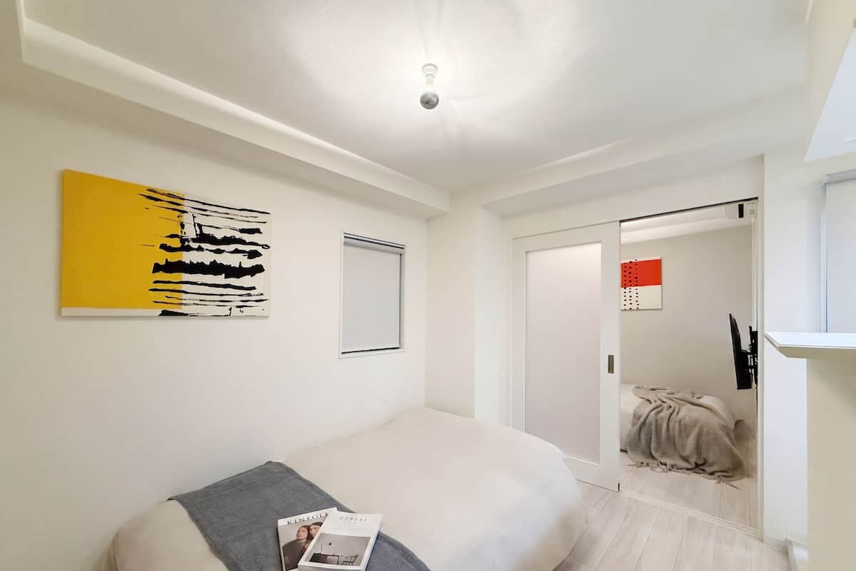 Quarto moderno com cama, janela, porta que dá para outro espaço e parede com uma obra de arte amarela.