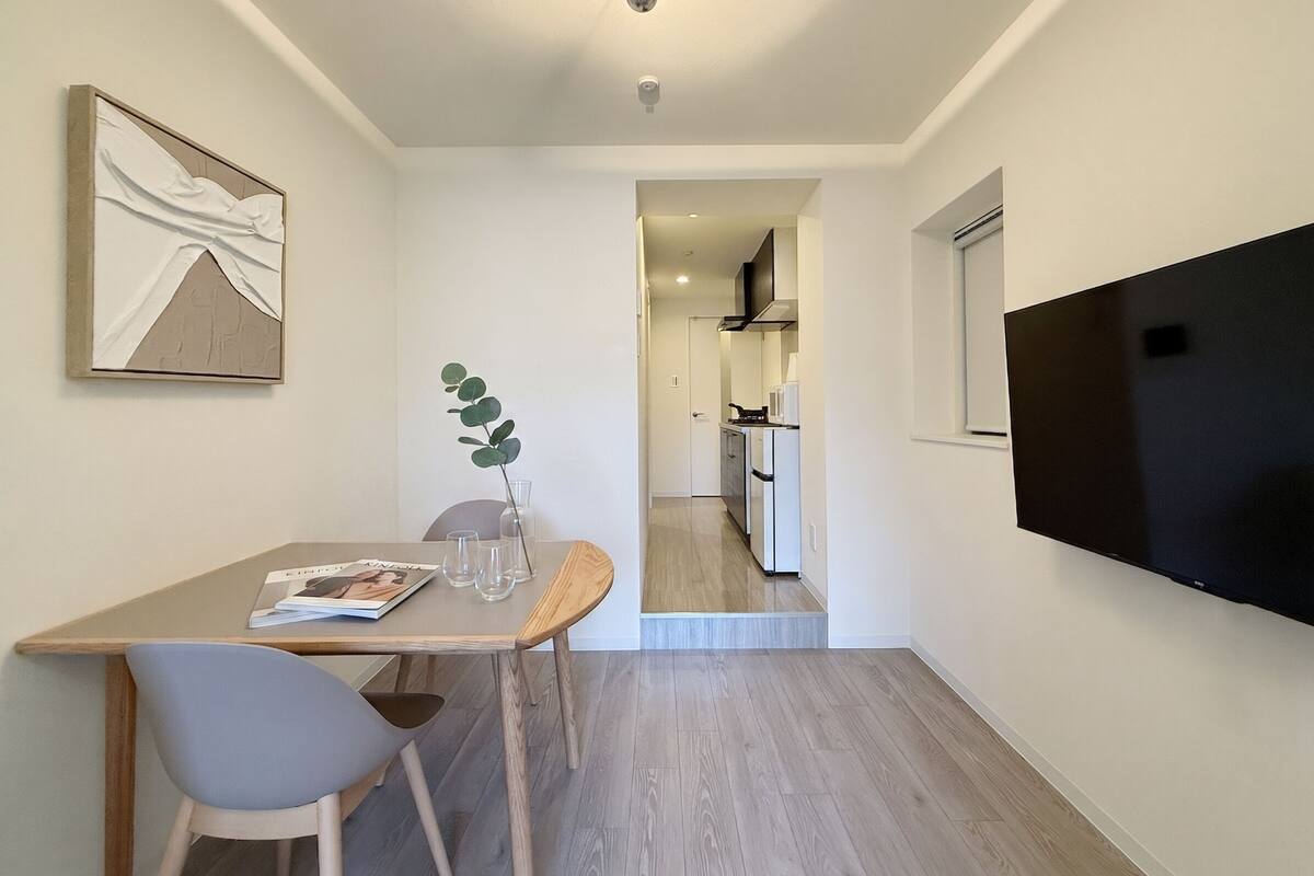 Uma cozinha moderna com televisão de tela plana, uma sala de jantar com mesa e cadeiras, e um corredor que leva a uma sala de estar.