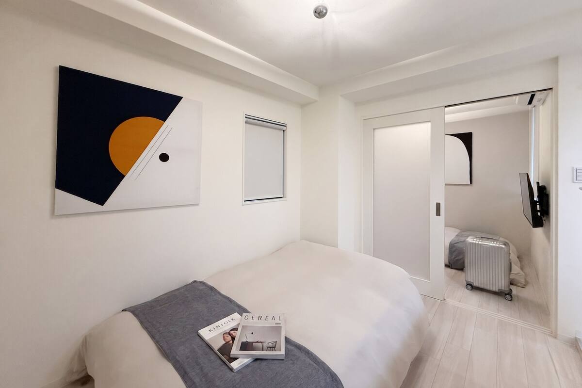 Quarto de hotel moderno com uma cama grande, uma obra de arte na parede, um radiador e uma porta que dá para outro quarto.