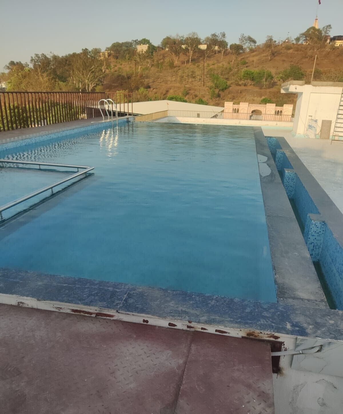 Piscina com vista desobstruída da paisagem ao redor, incluindo árvores e um edifício distante.