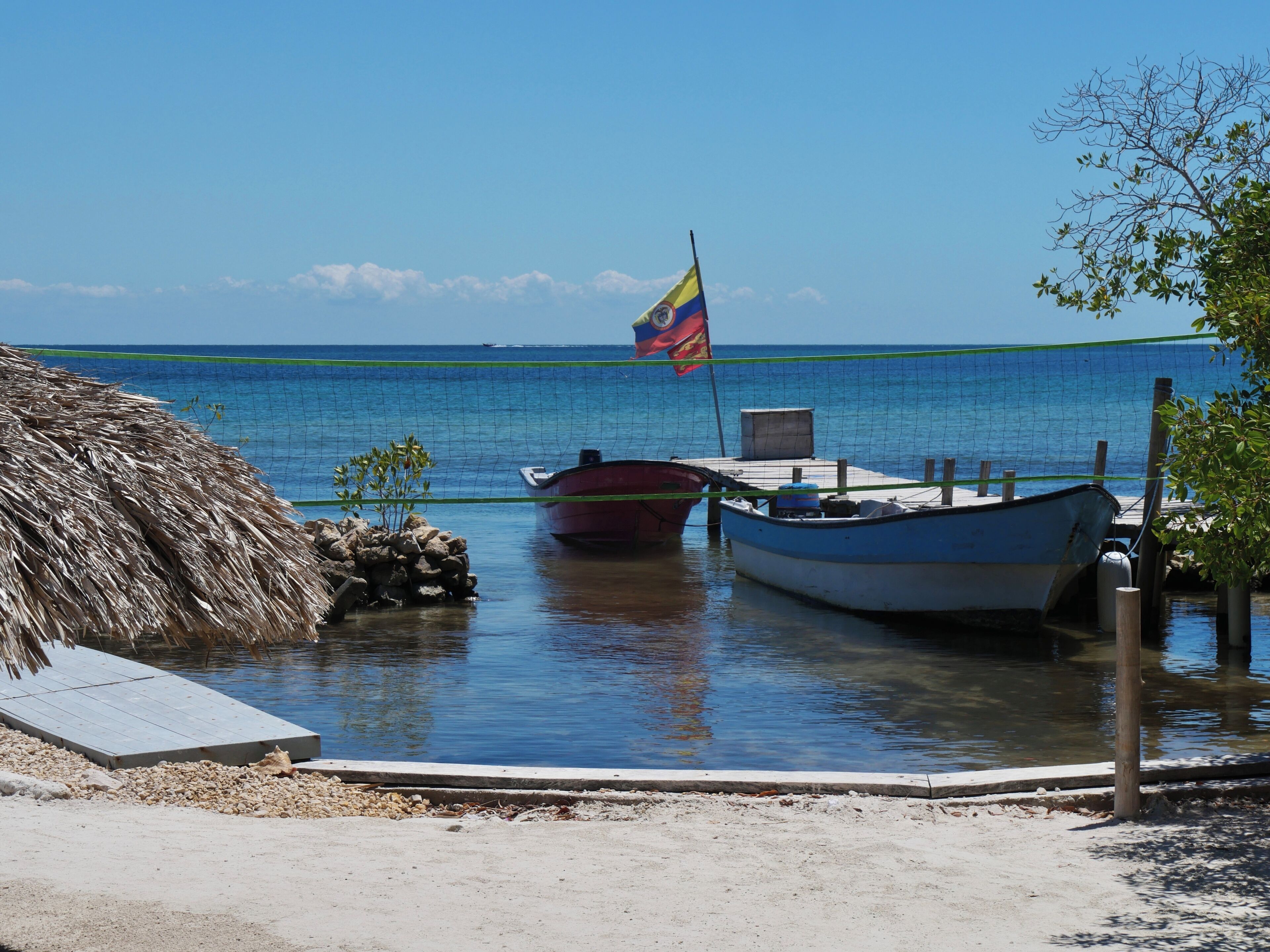 Uma praia com uma cabana de palha, um cais com barcos e um céu azul límpido.