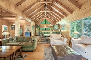 Interior de uma cabana de tronco com sala de jantar, cozinha e sala de estar, mobiliada com sofás e uma mesa de centro.
