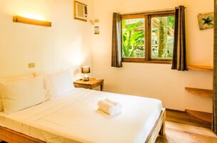 Quarto de hotel com cama, mesa de cabeceira, luminária, janela com cortinas e prateleira de madeira.