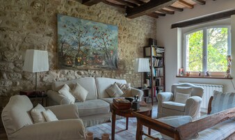 Um quarto com paredes de pedra, um sofá, poltronas, uma estante de livros e um quadro.