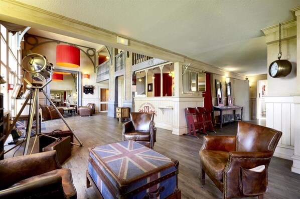 Um hall de hotel espaçoso com poltronas de couro, uma mala antiga e um espaço de bar.