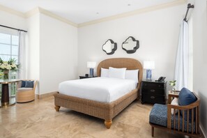 Um quarto espaçoso com uma cama grande, uma mesinha de cabeceira, uma cadeira e uma pequena mesa com luminária.