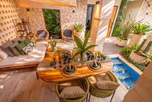 Uma área externa com mesa de madeira, cadeiras e uma piscina pequena.