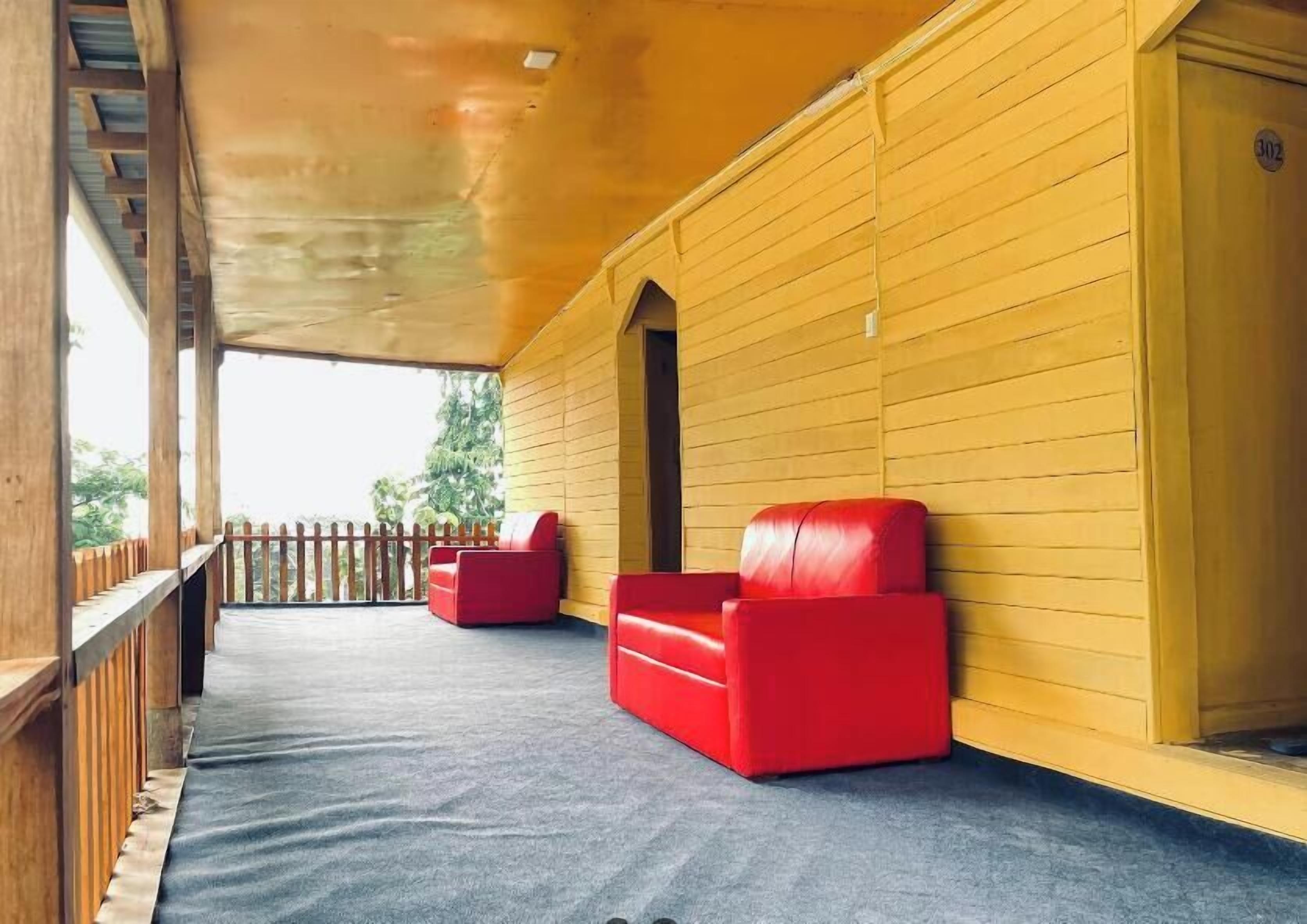 Um espaço coberto ao ar livre com paredes de madeira, um sofá vermelho e uma pequena mesa.